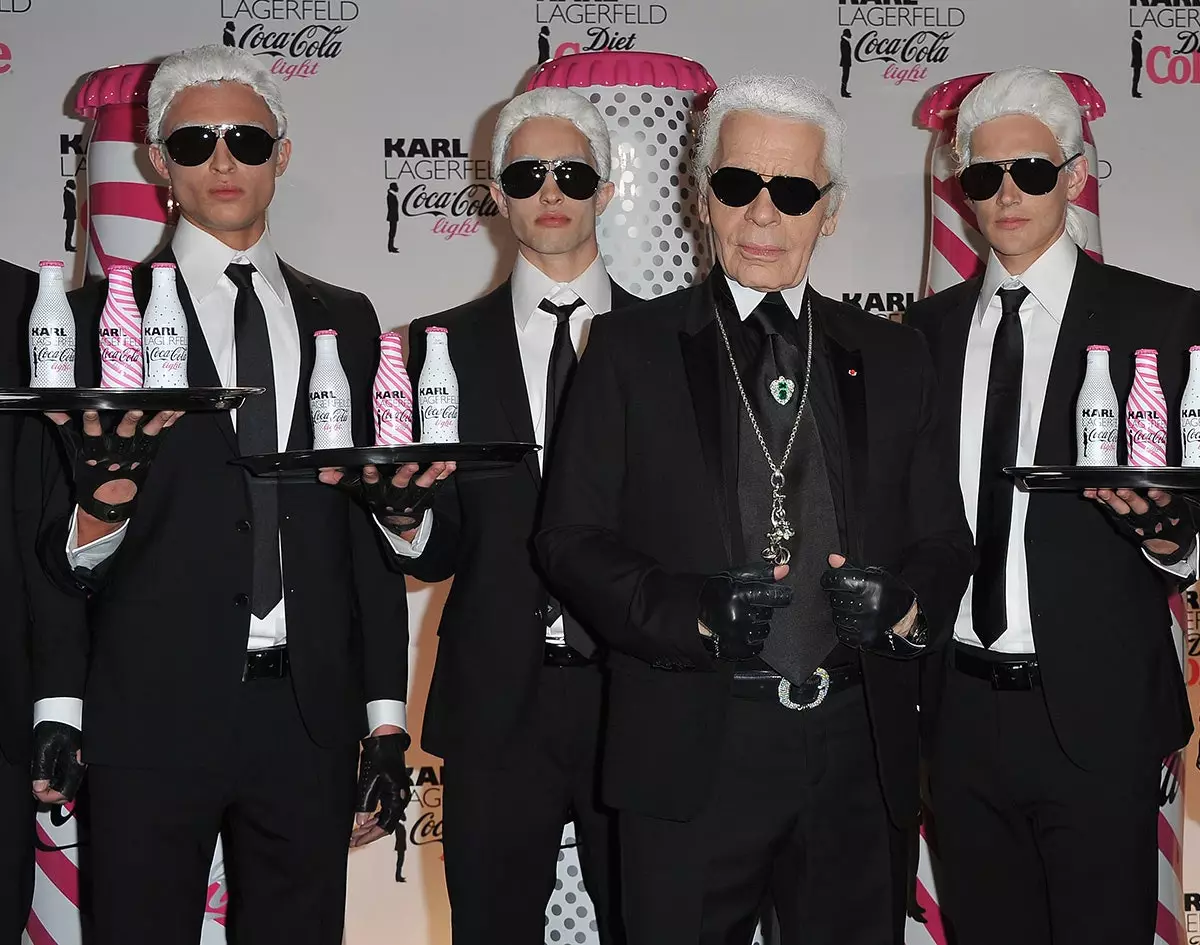 Lagerfeld circondato da doppiette e bottiglie di bibite che presenta la sua collaborazione con CocaCola.