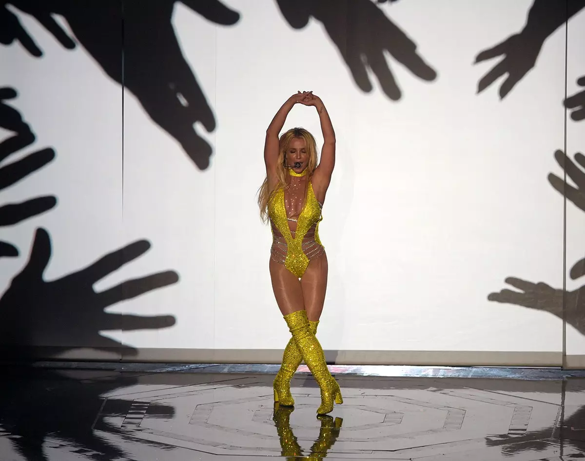 Britney Spears tańczy w otoczeniu wielu rąk, które nie kupiły jej albumu.