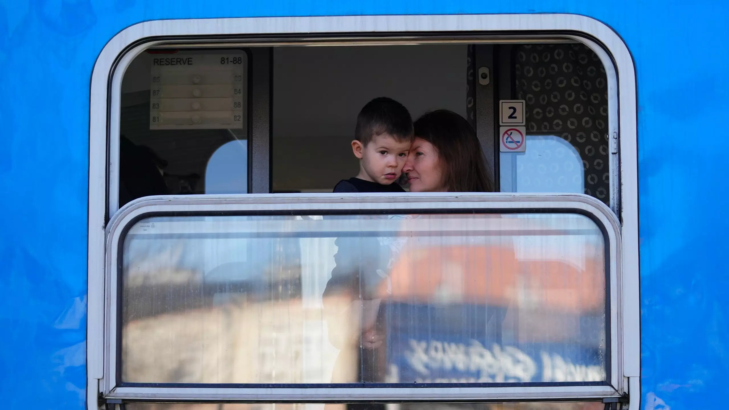 Egy nő gyermekkel a karján Ukrán menekültek várják, hogy induljanak Prágába a przemysli pályaudvaron...